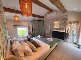 Quarto moderno com uma cama grande, chuveiro, toucador com espelho e janela com vista.