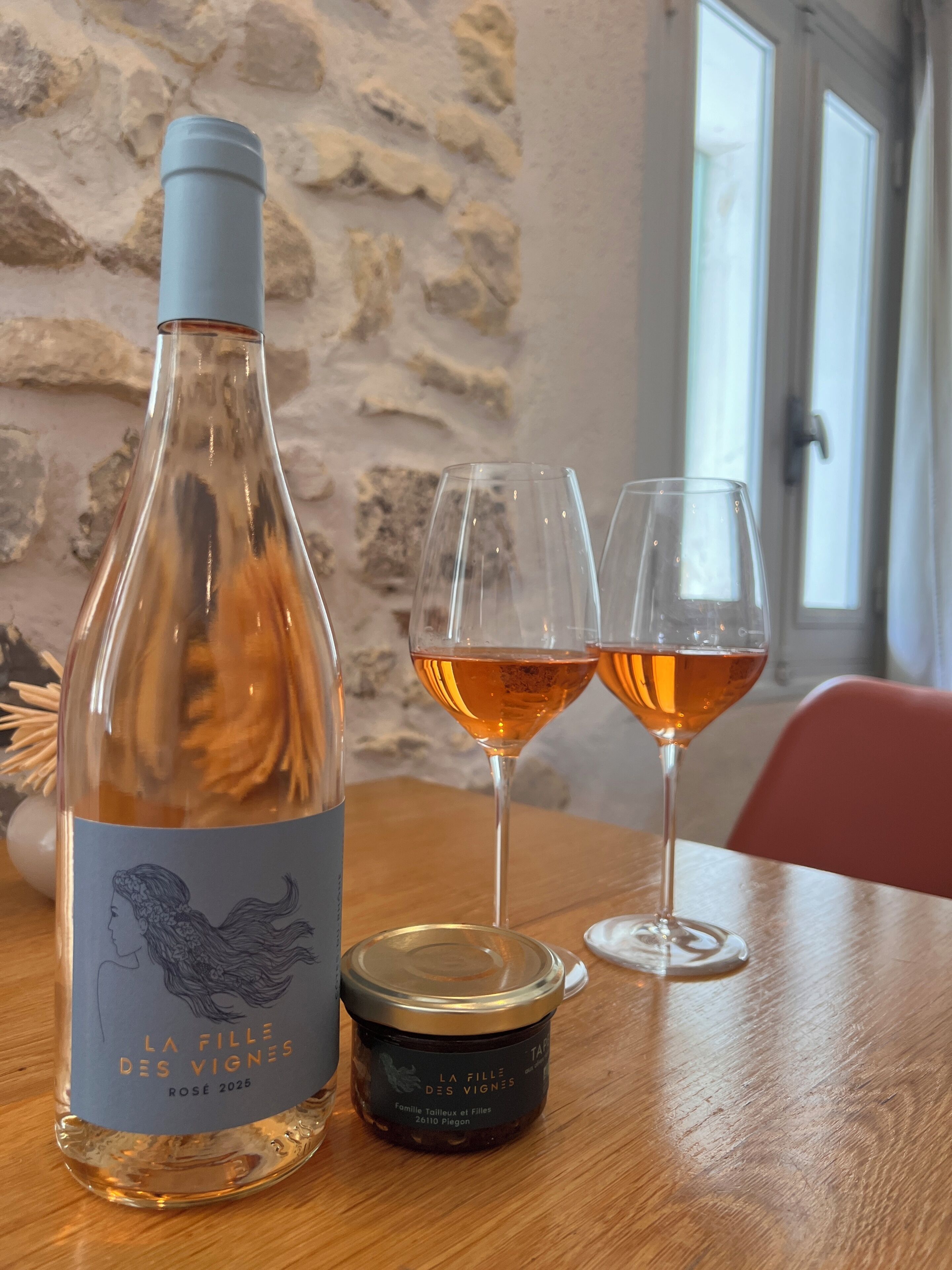 Uma garrafa de vinho, dois copos e um pequeno recipiente sobre uma mesa de madeira.