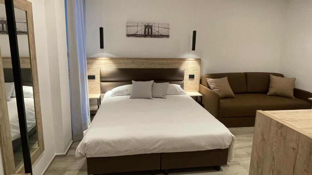Quarto de hotel com uma cama grande, cabeceira de madeira, sofá marrom e uma pequena mesa de madeira.