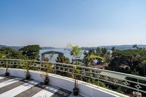 Uma varanda com plantas em vasos, vista para uma ponte e um corpo d'água.
