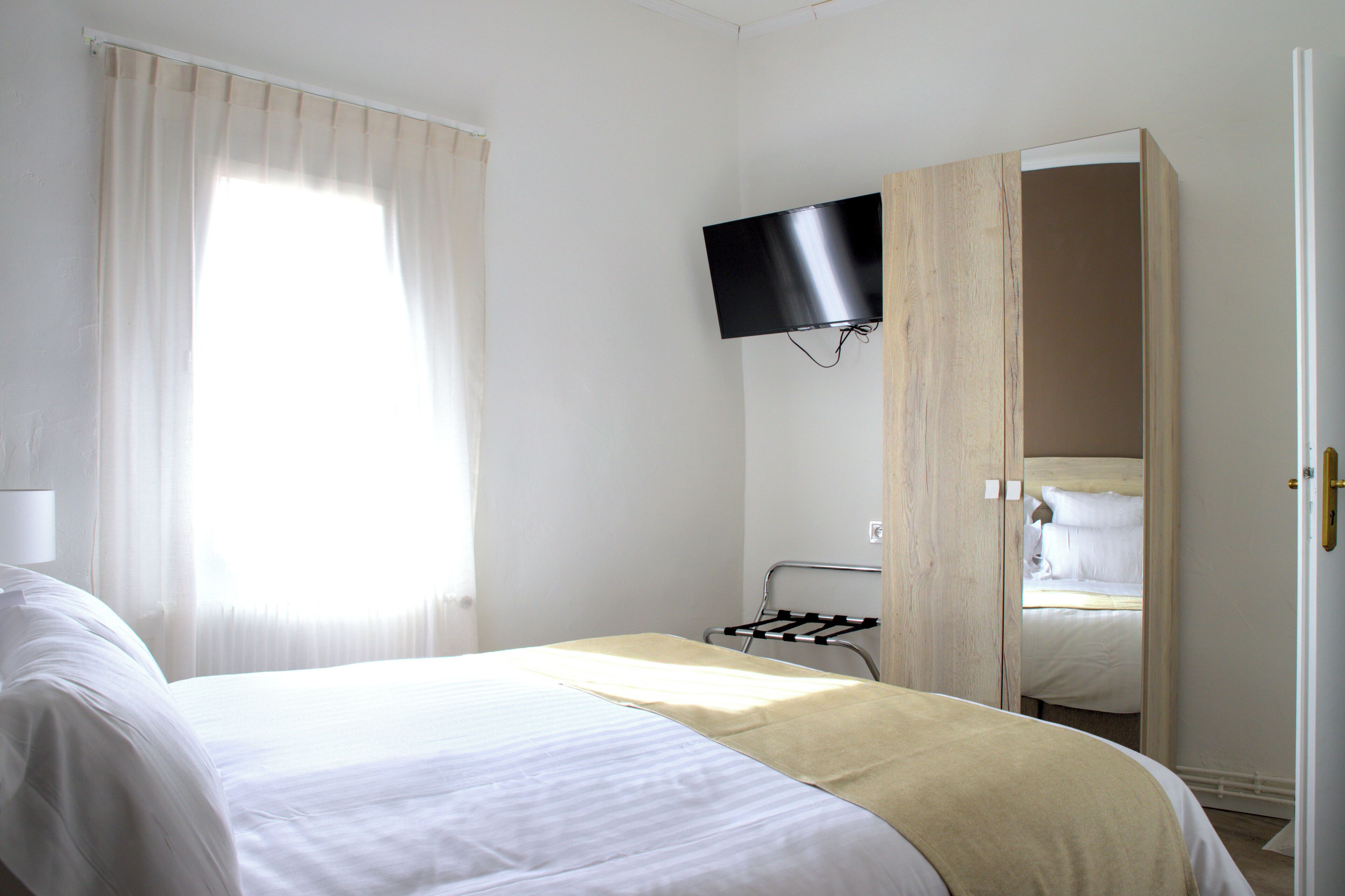 Quarto de hotel com cama, televisão fixada na parede e porta de acesso a outro espaço.