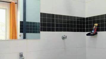 Casa de banho com uma pia branca, um espelho, um chuveiro e uma parede revestida a azulejos.