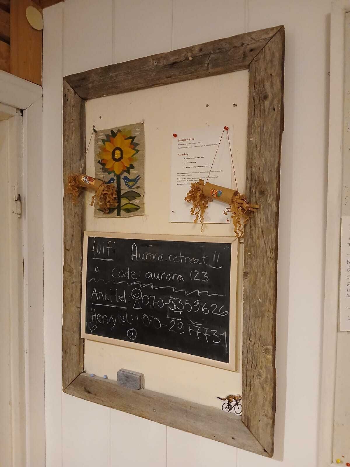 Quadro-negro com informações de contato de emergência, uma decoração de girassol e uma janela emoldurada em madeira.