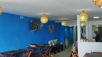 Restaurante com paredes azuis, mesas e cadeiras de madeira e luminárias decorativas penduradas.