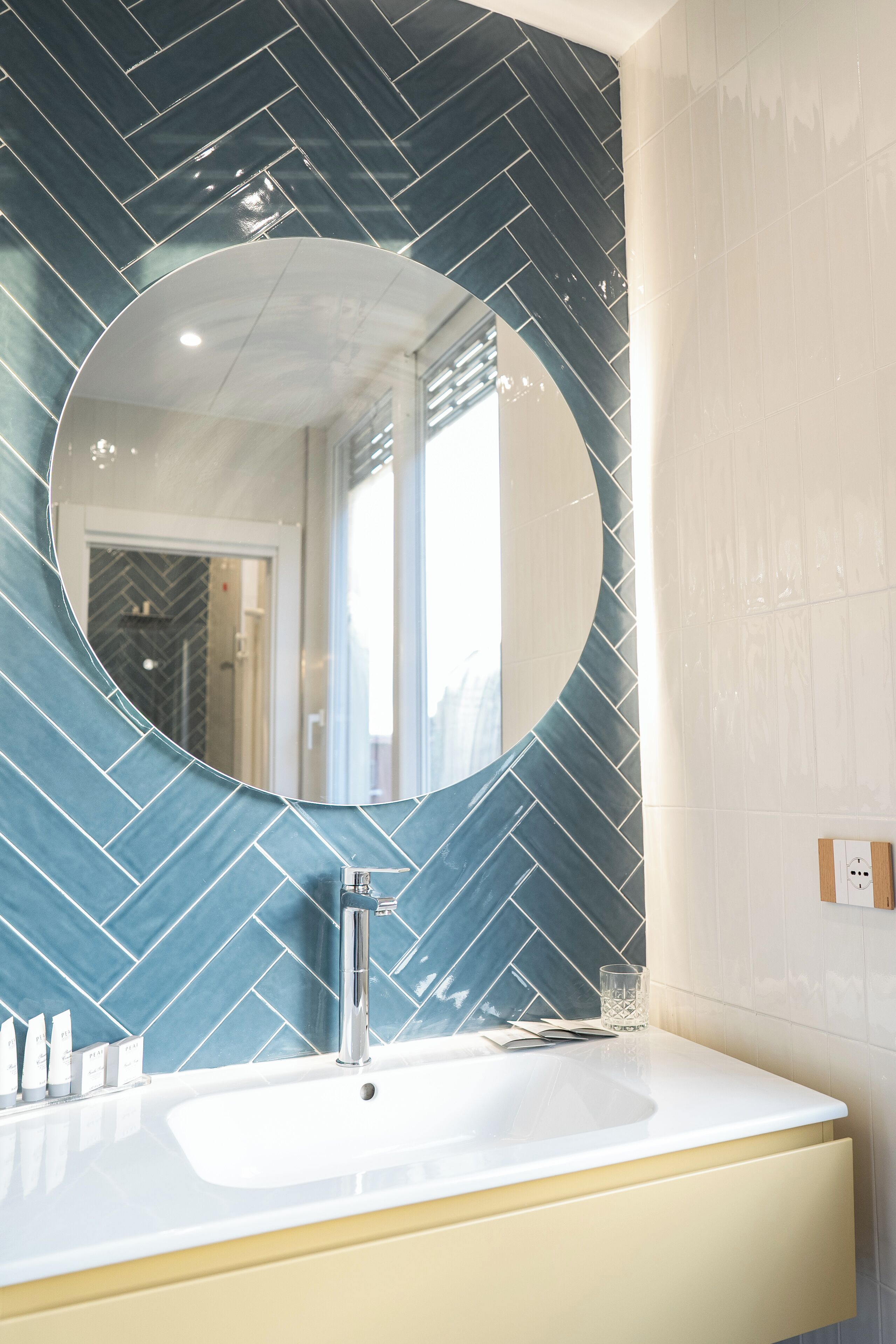 Casa de banho com lavatório branco, espelho e painel decorativo com padrão herringbone.