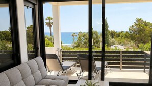 Uma sala de estar moderna com um sofá cinza, uma mesa de centro de madeira e vista para o mar.