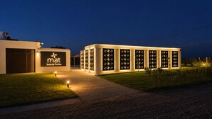 Um hotel moderno com uma placa indicando 'mat Suites By The Sea', apresentando um design clean com uma grande estrutura envidraçada e uma entrada bem iluminada.