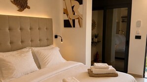 Um quarto moderno com uma cama grande, cabeceira, uma obra de arte pendurada na parede e uma porta que dá para um banheiro.