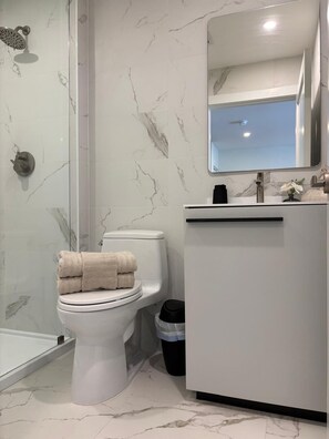 Um banheiro moderno com vaso sanitário, box de vidro e toucador com espelho.