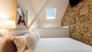 Quarto com cama, televisão na parede, claraboia e parede de pedra.