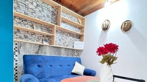 Quarto com sofá azul, mesa de jantar com cadeiras, parede de pedra e um claraboia.
