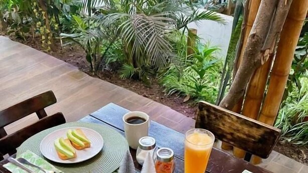 Mesa de madeira com um café da manhã, incluindo pratos de frutas, uma abacaxi e uma xícara de café.