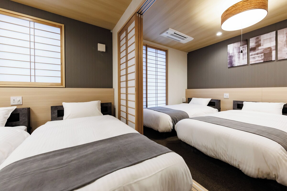 Quarto de hotel com três camas, porta deslizante, janela grande e ar-condicionado fixado na parede.