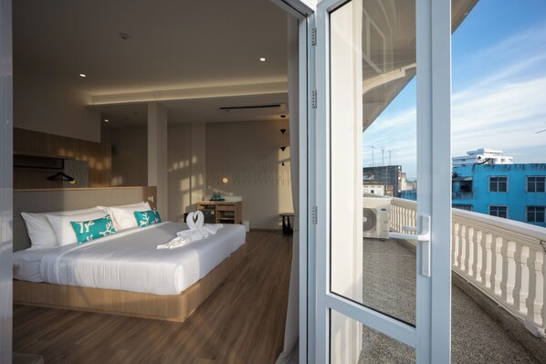 Quarto de hotel com cama grande, escrivaninha e varanda com vista para a cidade.