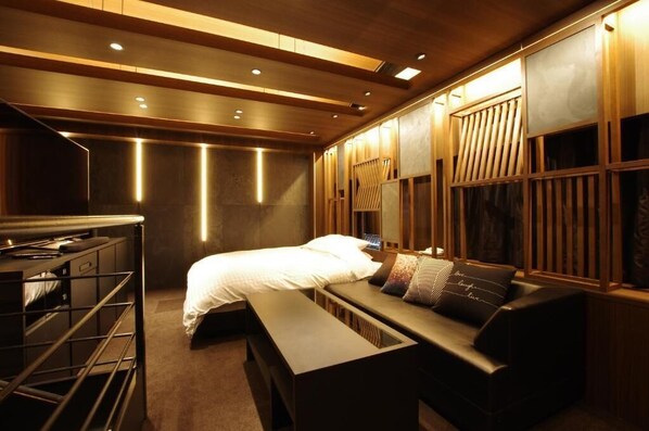 Quarto de hotel moderno com cama, sofá, escrivaninha e painéis de madeira embutidos.