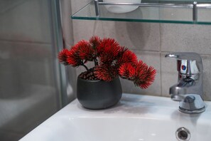 Casa de banho com uma prateleira de vidro, uma pia e uma planta em vaso com flores vermelhas.
