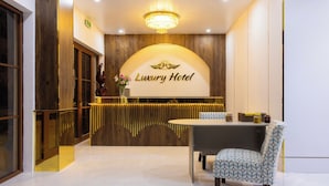 Uma área de recepção com uma placa que diz 'Luxury Hotel', um candelabro, um balcão de atendimento e uma cadeira estampada.