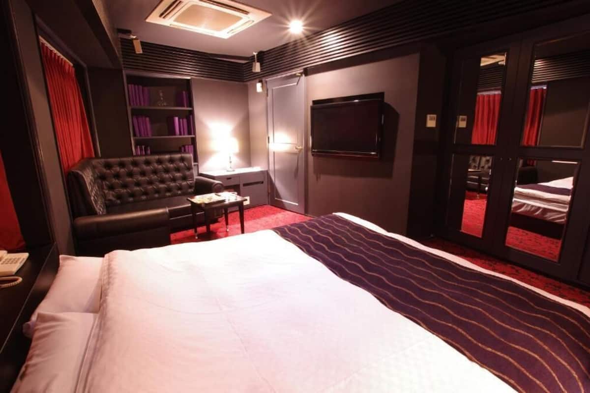 Quarto de hotel com cama, escrivaninha, cadeira, televisão e estante.