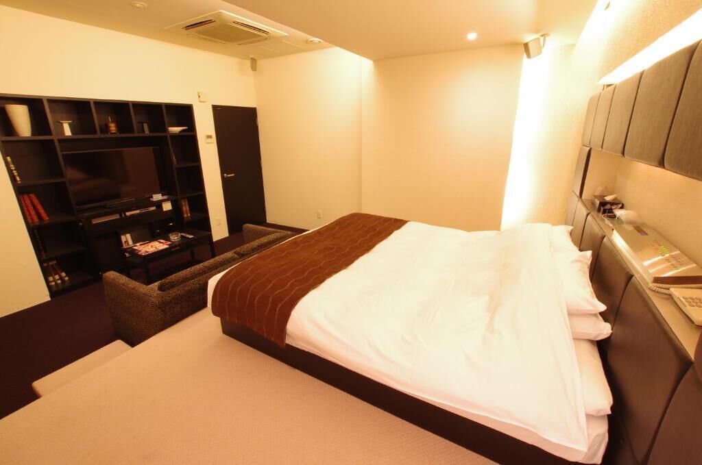Quarto de hotel com cama, televisão, escrivaninha e armário.