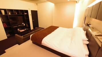 Quarto de hotel com cama, televisão, escrivaninha e armário.