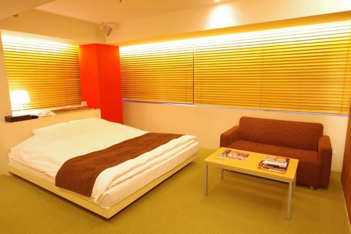 Quarto de hotel com cama, sofá, uma mesinha e janela com persianas.