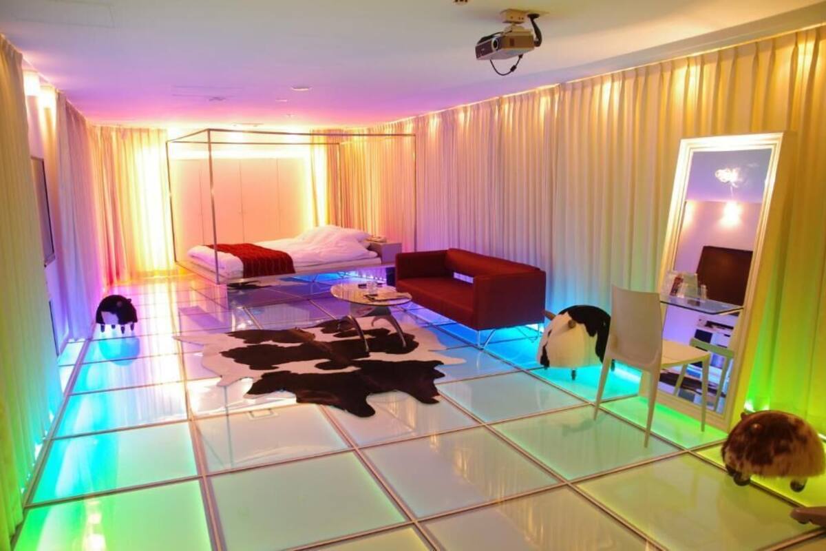 Quarto de hotel moderno com piso de vidro, uma cama, um sofá vermelho e um espaço de jantar.