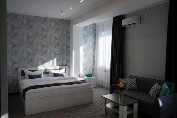 Quarto de hotel moderno com uma cama, um sofá, uma mesinha e um aparelho de ar condicionado.