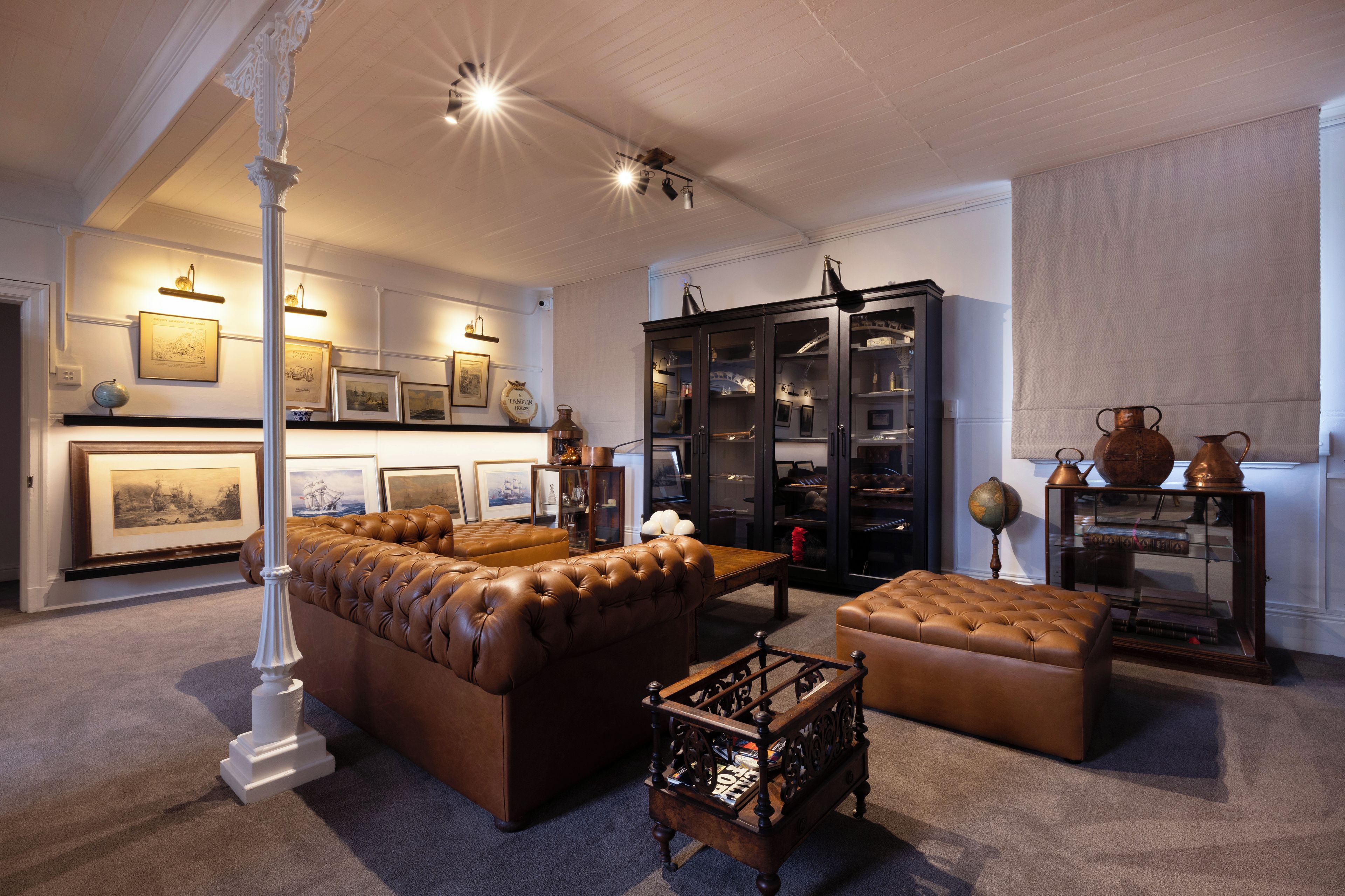 Uma sala de estar espaçosa com um amplo sofá de couro marrom, uma mesa de centro de madeira e um armário de madeira escura com portas de vidro.