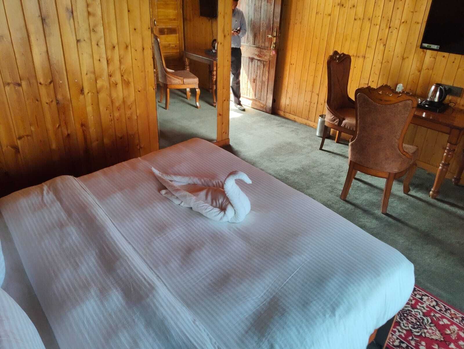 Um quarto com uma cama, uma cadeira de madeira, uma escrivaninha e uma televisão.