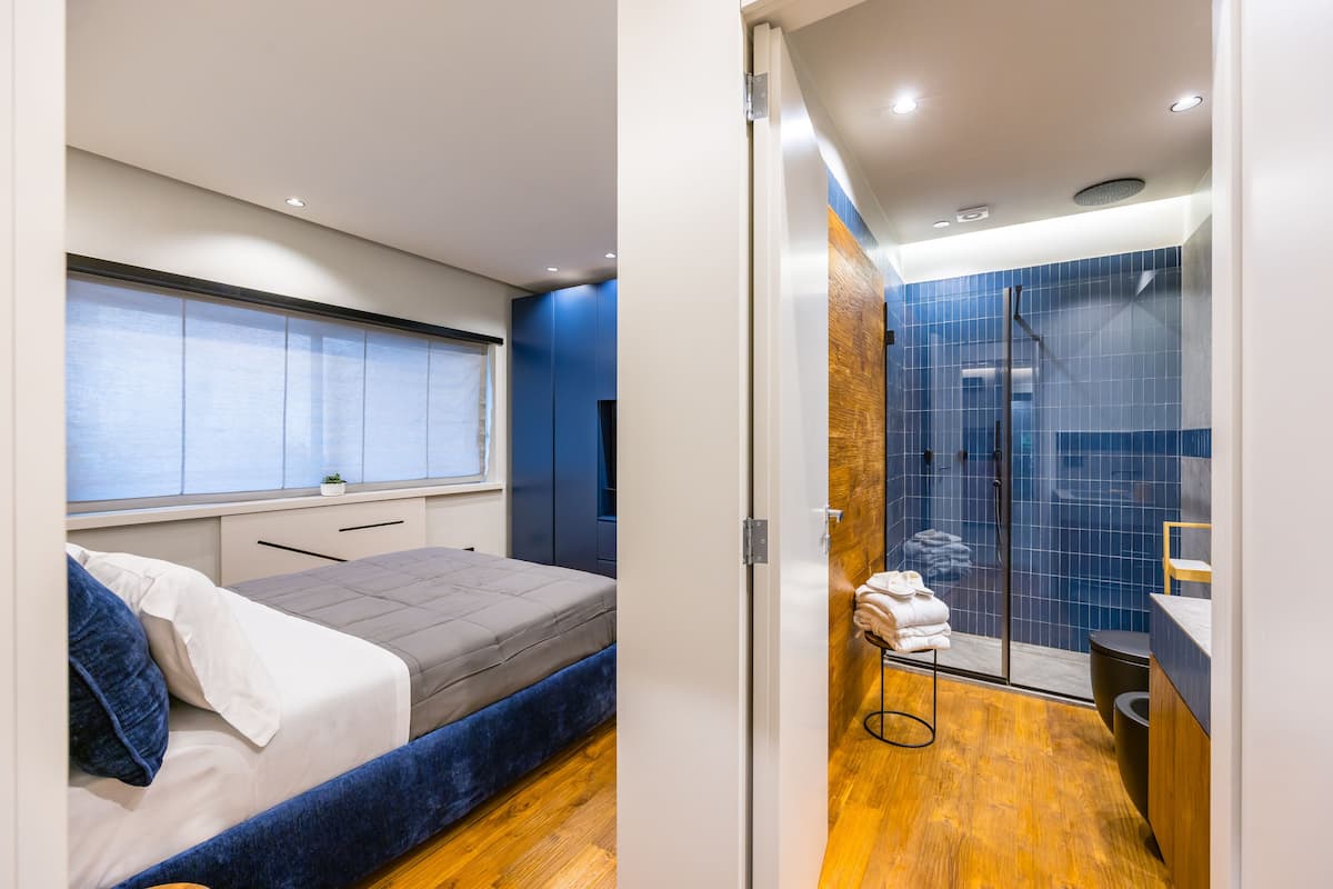 Quarto moderno com cama, janela e banheiro com chuveiro e pia.
