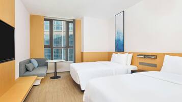 Quarto de hotel com duas camas, um sofá, uma mesinha e uma janela grande.