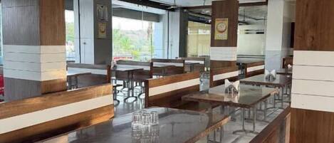Uma cafeteria moderna com mesas comunitárias grandes, bancos e ventiladores de teto.