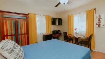 Quarto com cama, escrivaninha com cadeira, ventilador de teto e televisão na parede.