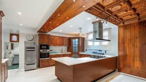 Uma cozinha moderna com armários de madeira, uma ilha central, eletrodomésticos de aço inoxidável e teto decorativo.