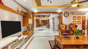 Uma sala de estar espaçosa com televisão de tela plana, prateleiras de madeira, mesa de centro de mármore e ventilador de teto.