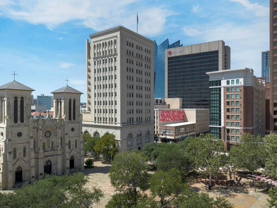 Paisagem urbana com um edifício histórico, uma torre de sino e um arranha-céu moderno ao fundo.
