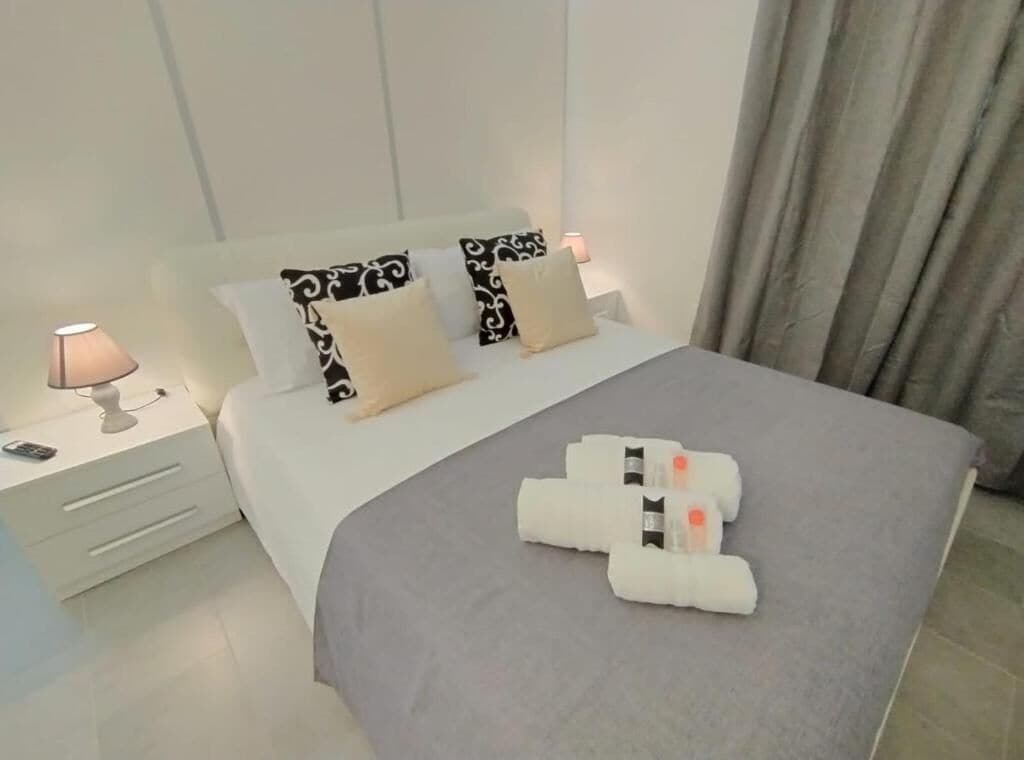Cama bem arrumada com travesseiros, abajur e telefone na mesa de cabeceira.