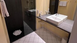Um banheiro moderno com chuveiro em box de vidro, um espelho grande e uma pia branca.