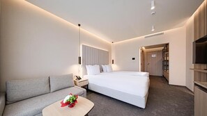 Quarto de hotel moderno com uma cama, um sofá, uma mesinha com um arranjo floral e uma televisão.