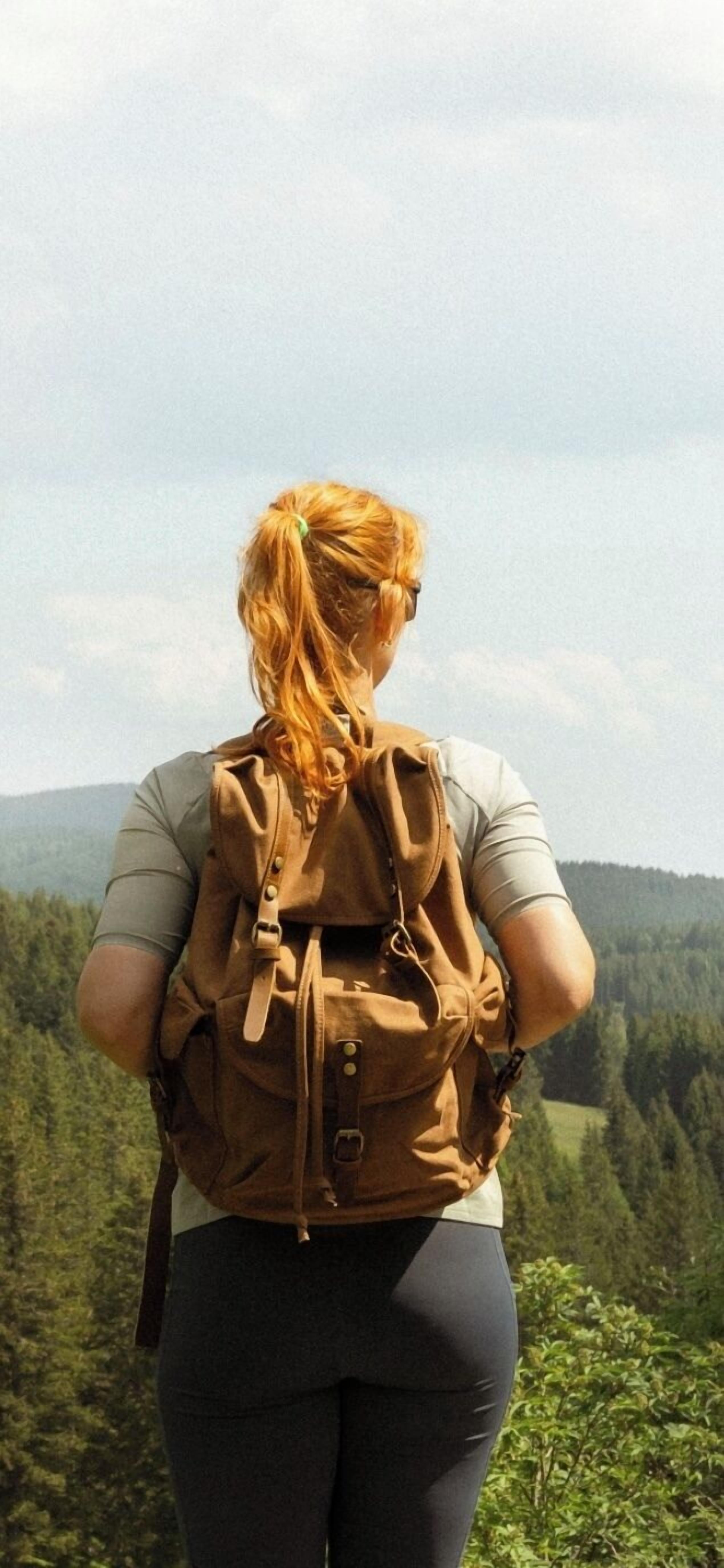 Uma pessoa com mochila apreciando a vista de uma paisagem arborizada.