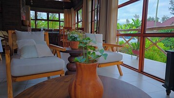 Quarto com sofá, cadeiras, mesa de jantar e uma grande janela com vista para o verde.
