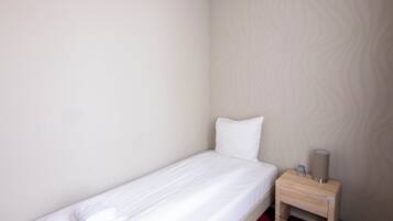 Uma cama de solteiro com colchão e travesseiro brancos, um criado-mudo de madeira com abajur e uma parede com textura.