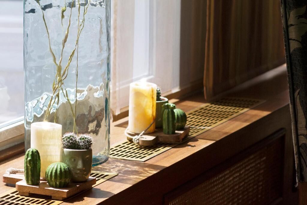 Um peitoril de janela com um vaso de vidro, velas e pequenas plantas em vasos.