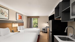 Quarto de hotel com duas camas, cozinha compacta, janela com vista e obras de arte nas paredes.