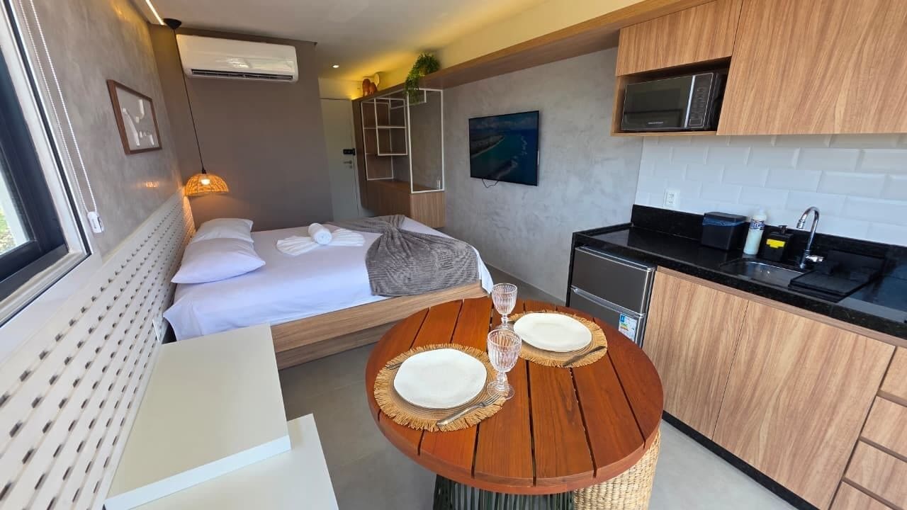 Quarto compacto com uma cama, uma mesa de jantar com pratos e copos, micro-ondas e pia.