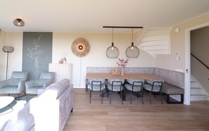 Uma sala de estar moderna com um sofá, uma mesa de jantar com cadeiras, uma grande obra de arte na parede e uma escada.