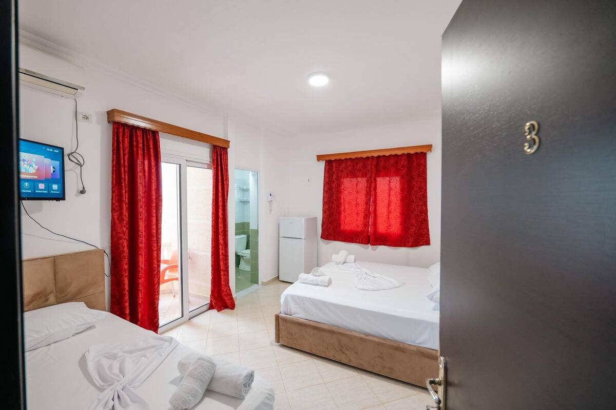 Quarto de hotel com cama, televisão, escrivaninha e banheiro visível através de uma porta aberta.