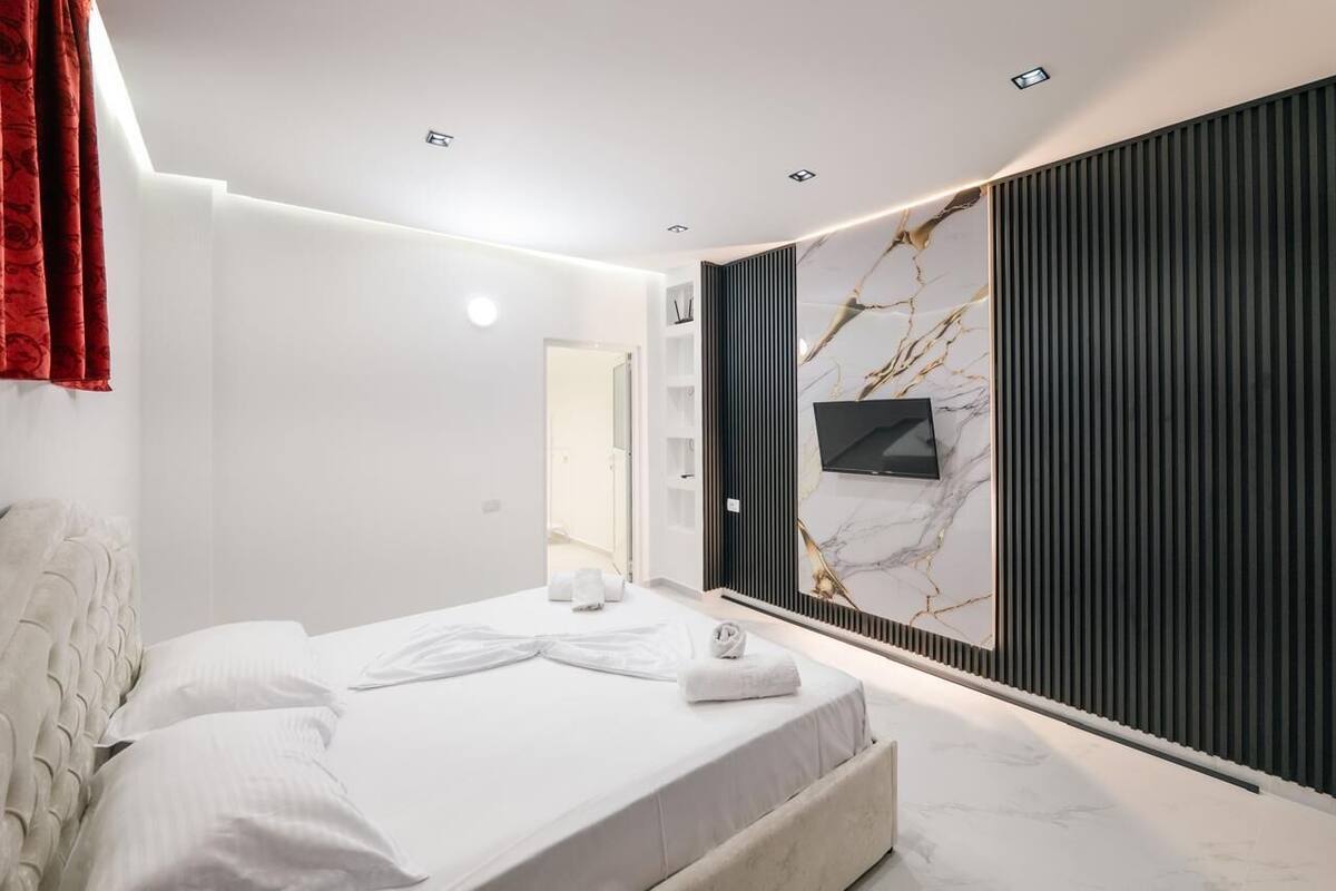 Quarto moderno com cama, TV e parede de mármore.