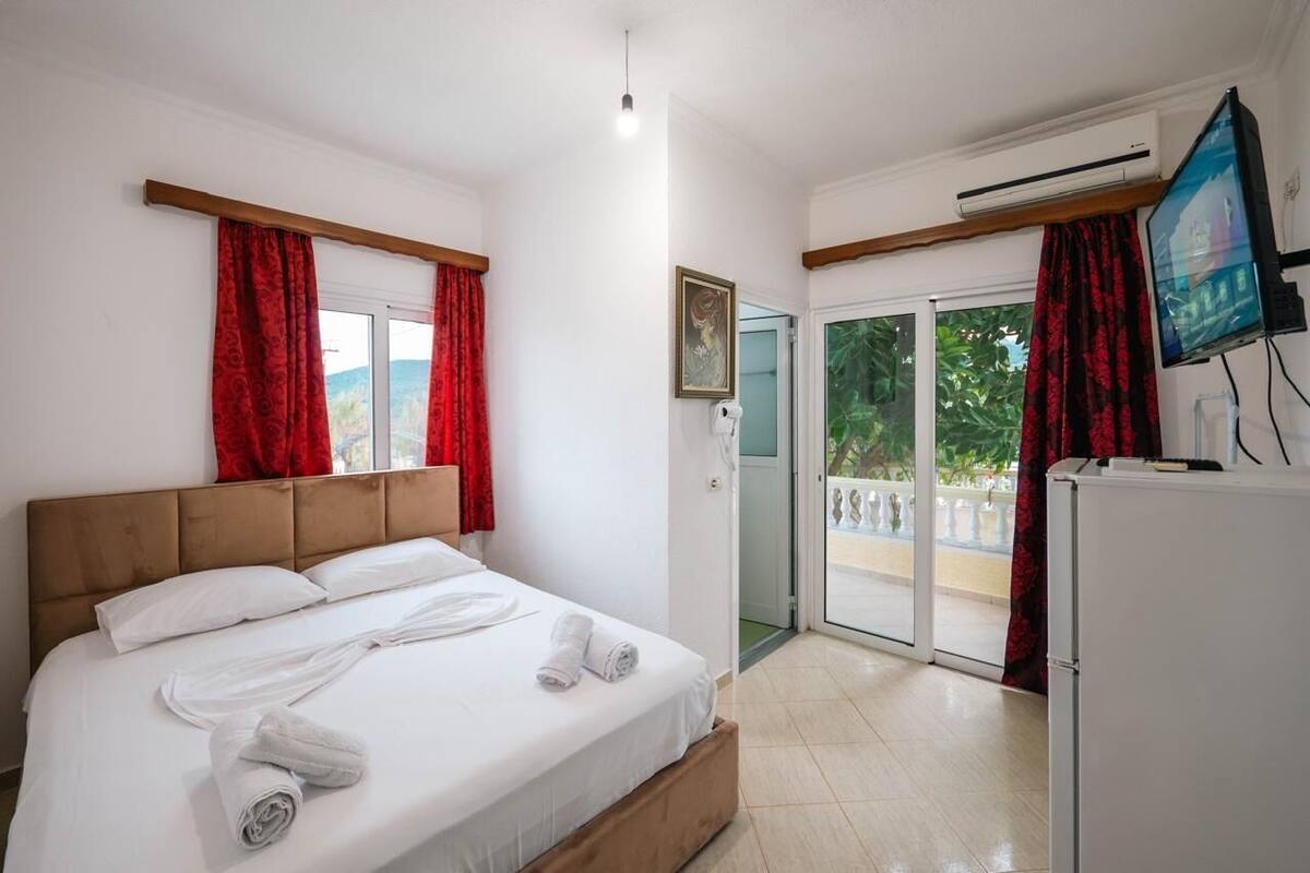 Quarto de hotel com cama, televisão e porta de vidro deslizante para uma varanda.