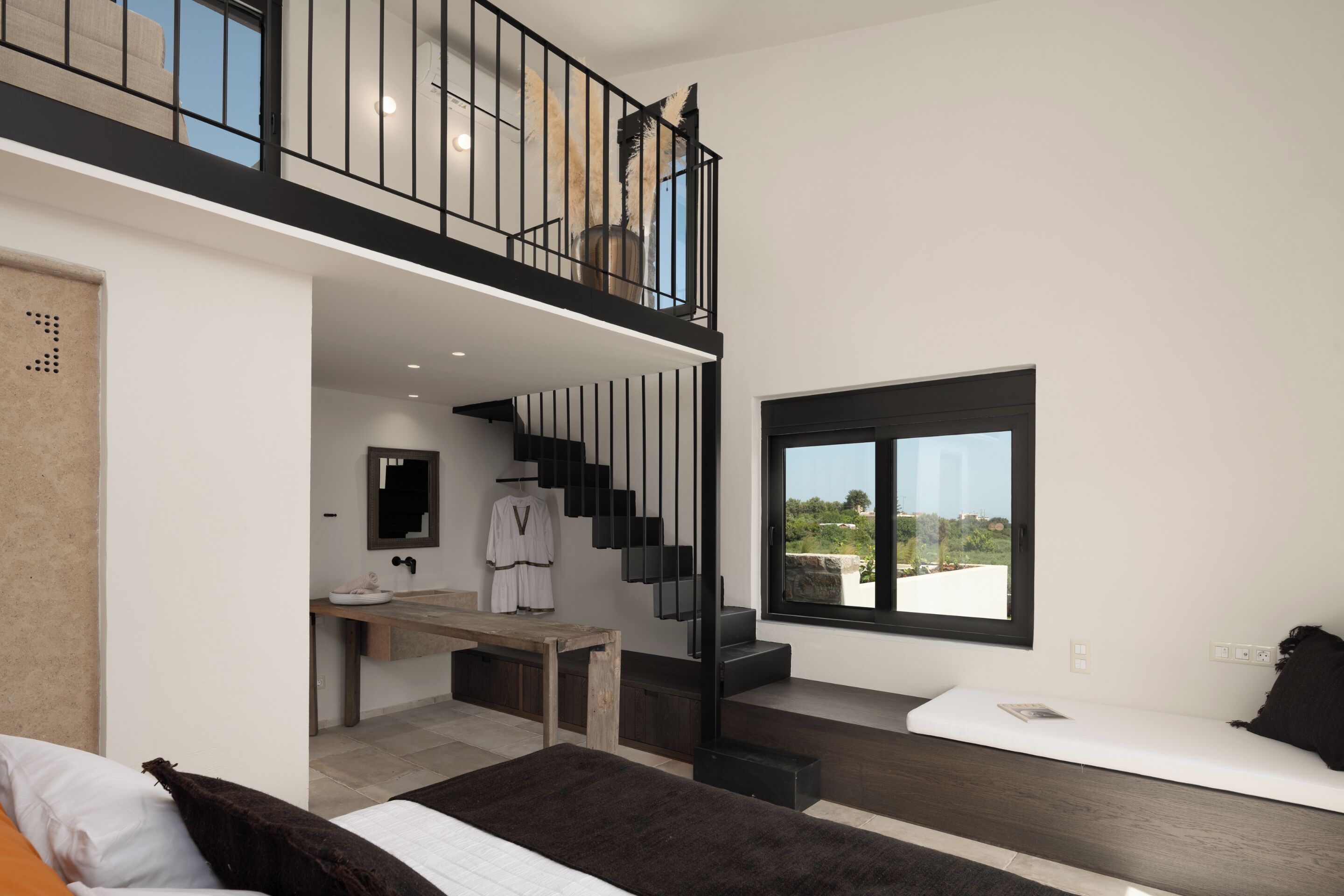 Quarto moderno com cama grande, escrivaninha de madeira, escada e vista para o exterior.